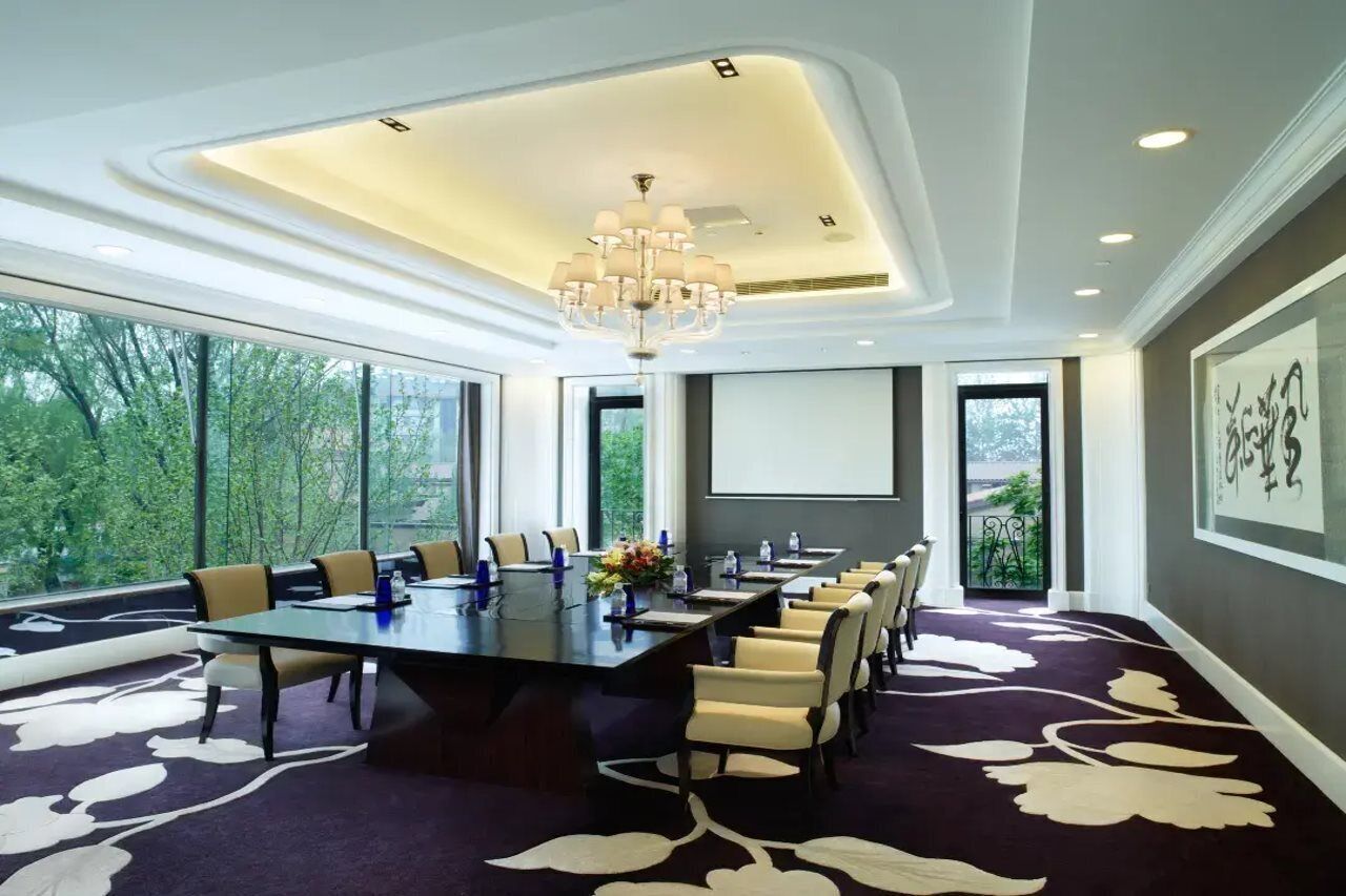 Uma sala de conferência com uma mesa grande, cadeiras, uma tela de projetor e um candelabro.