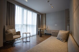 Quarto de hotel moderno com sofá, poltrona, mesa pequena e escrivaninha.