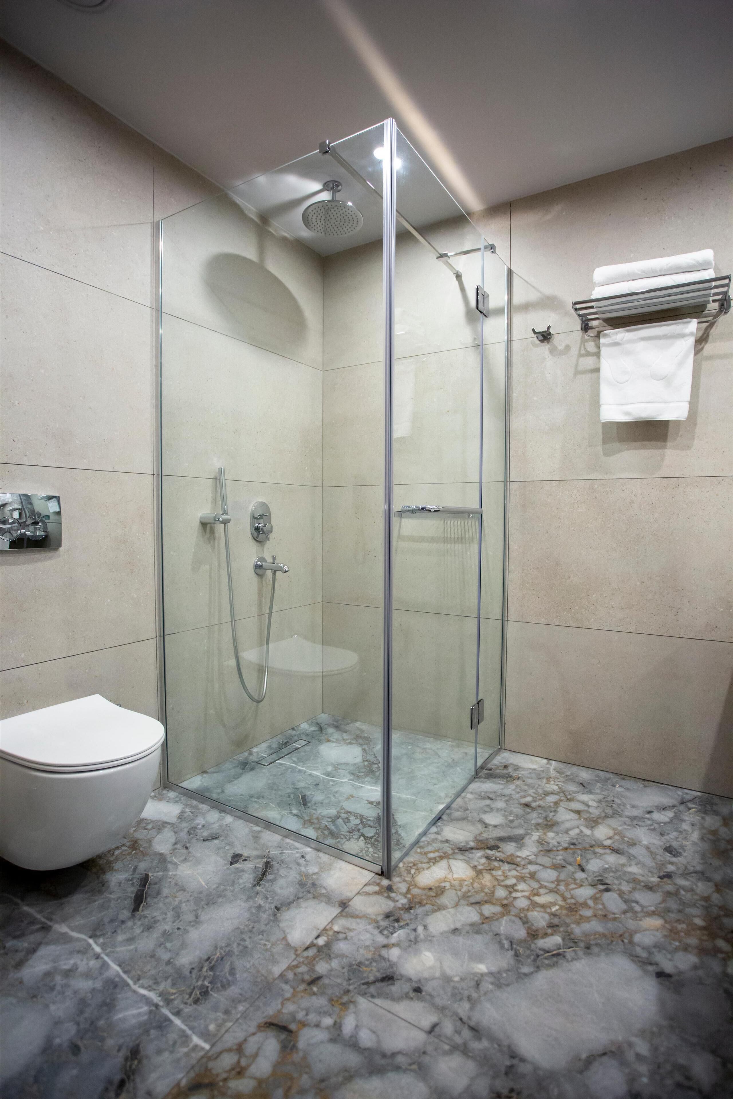 Uma casa de banho moderna com chuveiro de vidro, sanita e chão em mármore.