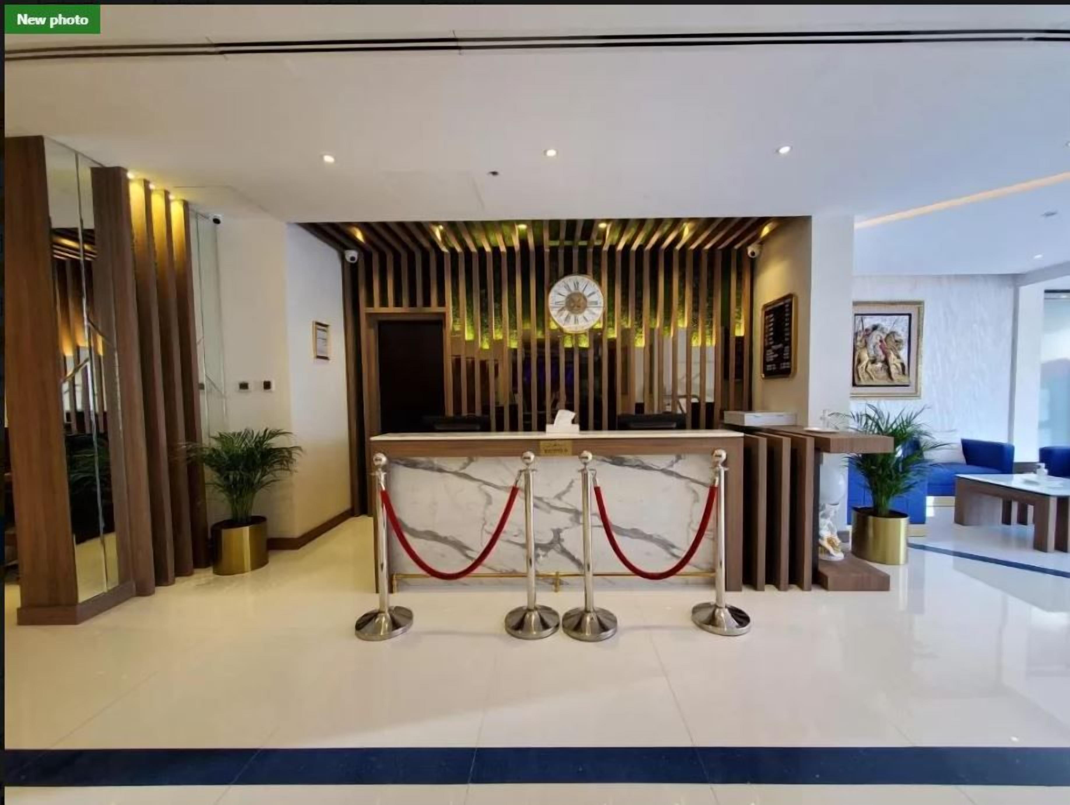 Uma área de recepção de hotel com balcão de mármore, um relógio e uma barreira de corda vermelha.