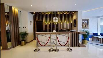 Uma área de recepção de hotel com balcão de mármore, um relógio e uma barreira de corda vermelha.