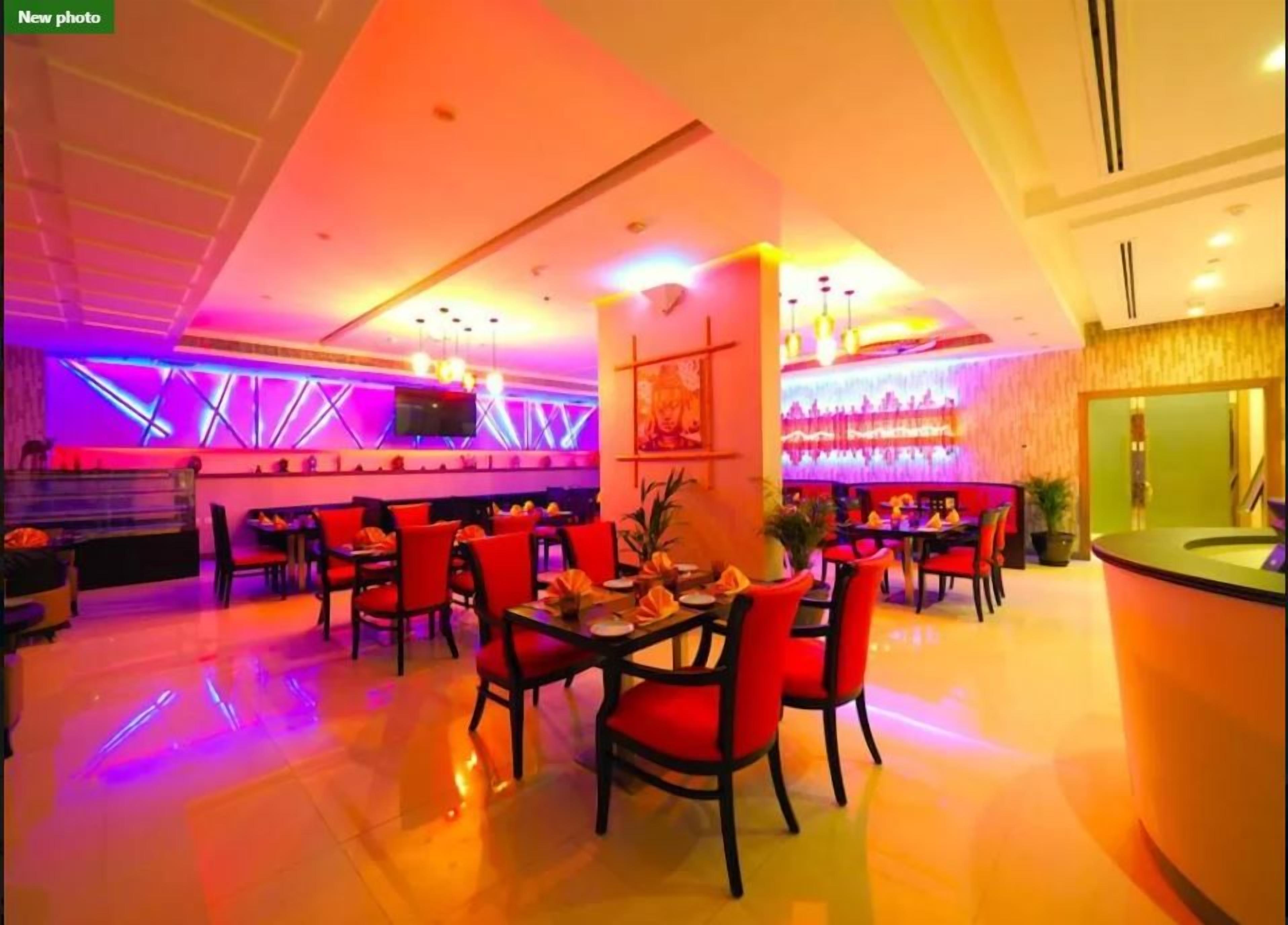 Restaurante com cadeiras vermelhas, área de bar e uma tela de televisão na parede.