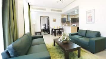 Sala de estar com dois sofás, uma mesa de centro e um tapete. Ao fundo, há um espaço de refeições com uma mesa e cadeiras.