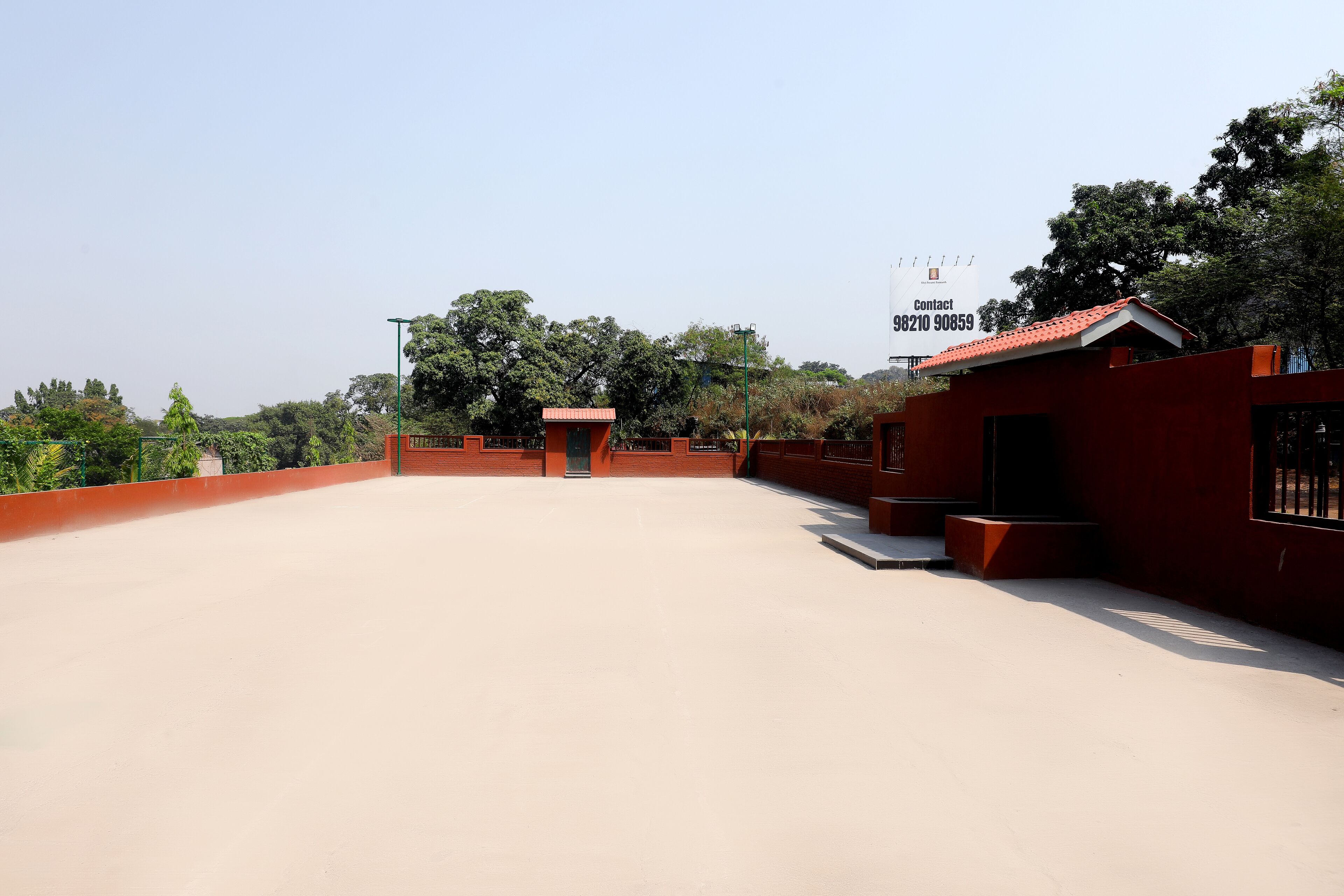 Terraço no telhado com um edifício vermelho, um número de contato e árvores ao fundo.
