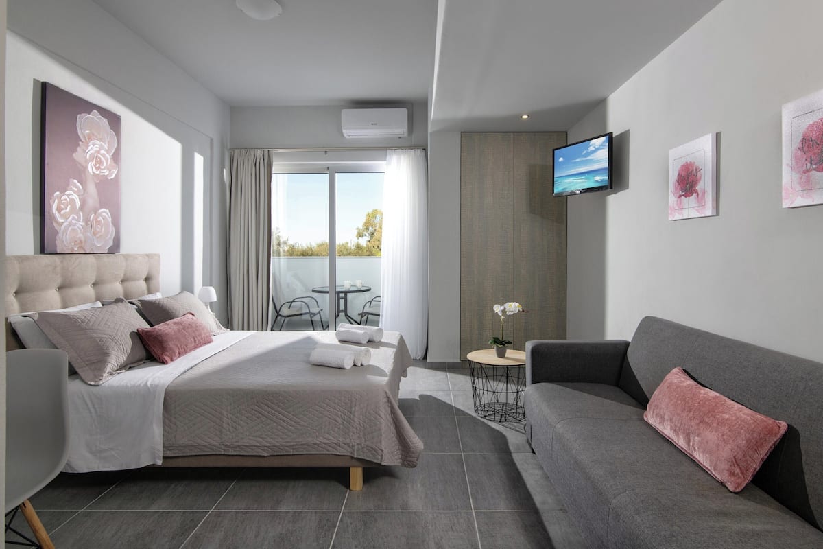 Quarto de hotel moderno com cama, sofá, televisão e varanda.