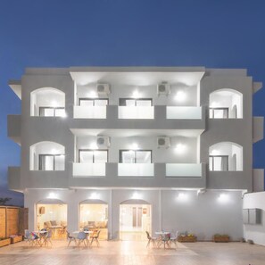 Um edifício com vários andares, varandas, amplas janelas e um pátio com mesas ao ar livre.