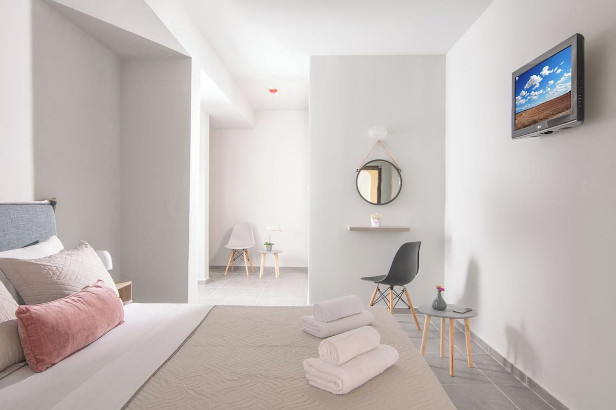 Quarto de hotel moderno com uma cama, televisão de tela plana, espelho redondo e uma mesinha com um vaso.