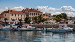 Uma marina com vários barcos atracados, um muro de pedra e edifícios com telhados de barro.