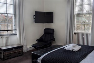 Quarto de hotel com cama, uma cadeira, uma televisão e uma mala.