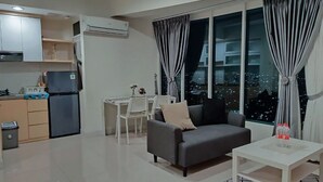 Uma sala de estar moderna com sofá, uma mesinha e um espaço de jantar com mesa e cadeiras. Há também uma cozinha com armários e uma geladeira.
