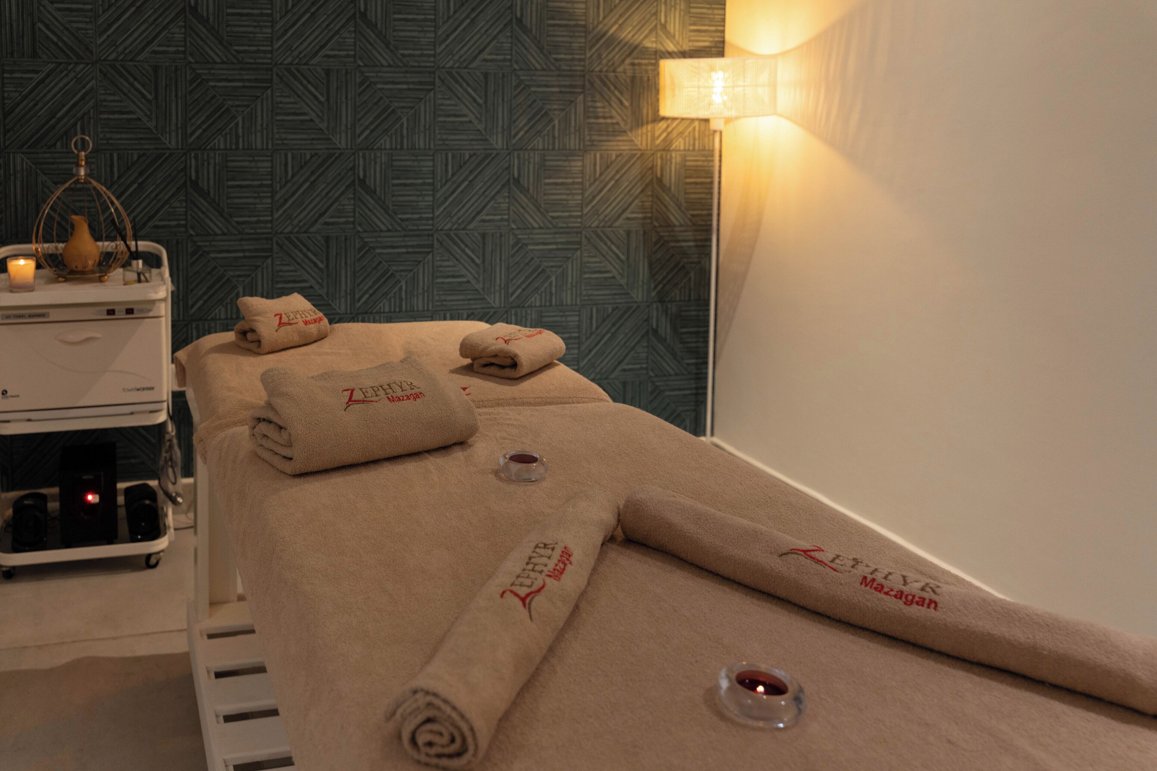 Mesa de massagem com toalhas e uma lâmpada em um quarto com papel de parede estampado.