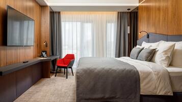 Quarto de hotel moderno com uma cama grande, uma escrivaninha com cadeira, televisão de tela plana e uma janela ampla com cortinas.