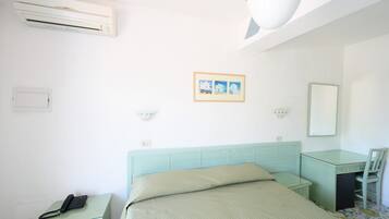 Quarto com cama, escrivaninha, cadeira, ar-condicionado, telefone, quadro emoldurado e espelho.