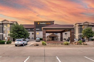 Um hotel Comfort Suites com entrada moderna, estacionamento e céu claro.
