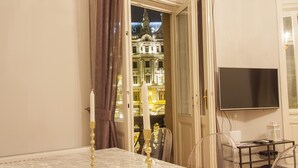 Uma sala de jantar com uma mesa de mármore, um candelabro e vista para um edifício histórico através de uma porta aberta.