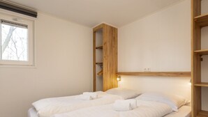 Quarto com duas camas, estantes de madeira, uma janela e luminária na parede.