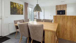 Uma sala de jantar moderna com uma mesa de madeira e quatro cadeiras, uma luminária pendente e uma janela grande com cortinas.