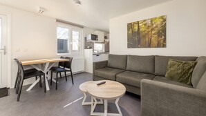 Uma sala de estar moderna com sofá, mesa de jantar com cadeiras, área de cozinha com micro-ondas e uma janela grande.