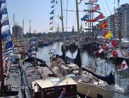 Marina com vários barcos atracados, cercada por edifícios e bandeiras.