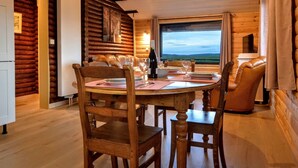 Uma sala de jantar acolhedora em uma cabana de madeira, com uma mesa para quatro pessoas, cadeiras de couro e vista para a paisagem através de uma grande janela.