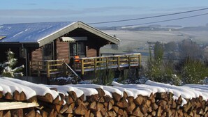 Uma cabana com deck de madeira e vista para uma paisagem nevada.