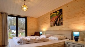 Quarto com painéis de madeira, uma cama grande, luminárias de cabeceira e um quadro de uma árvore.