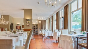 Um restaurante com várias mesas, toalhas brancas e cadeiras.