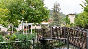 Uma ponte de madeira sobre um pequeno riacho, cercada por vegetação e um muro de pedra.