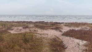 Paisagem costeira com um caminho de areia que leva ao oceano.