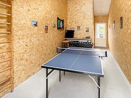Uma mesa de ping pong em um quarto com paredes de madeira, uma porta e uma janela.