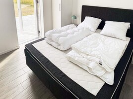 Quarto moderno com uma cama grande, mesa de cabeceira e vista para o exterior através de uma porta de vidro.