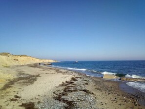 Uma praia com céu claro, mar calmo e costa rochosa.