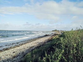Paisagem costeira com costa rochosa, vegetação e uma vista distante de um pequeno povoado.