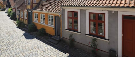 Rua de paralelepípedos ladeada por edifícios tradicionais em estilo europeu, com telhados inclinados e janelas salientes.
