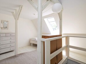 Quarto com teto inclinado, cômoda de madeira, cama e janela que oferece luz natural.