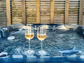 Uma banheira de hidromassagem com duas taças de vinho, cercada por ripas de madeira.