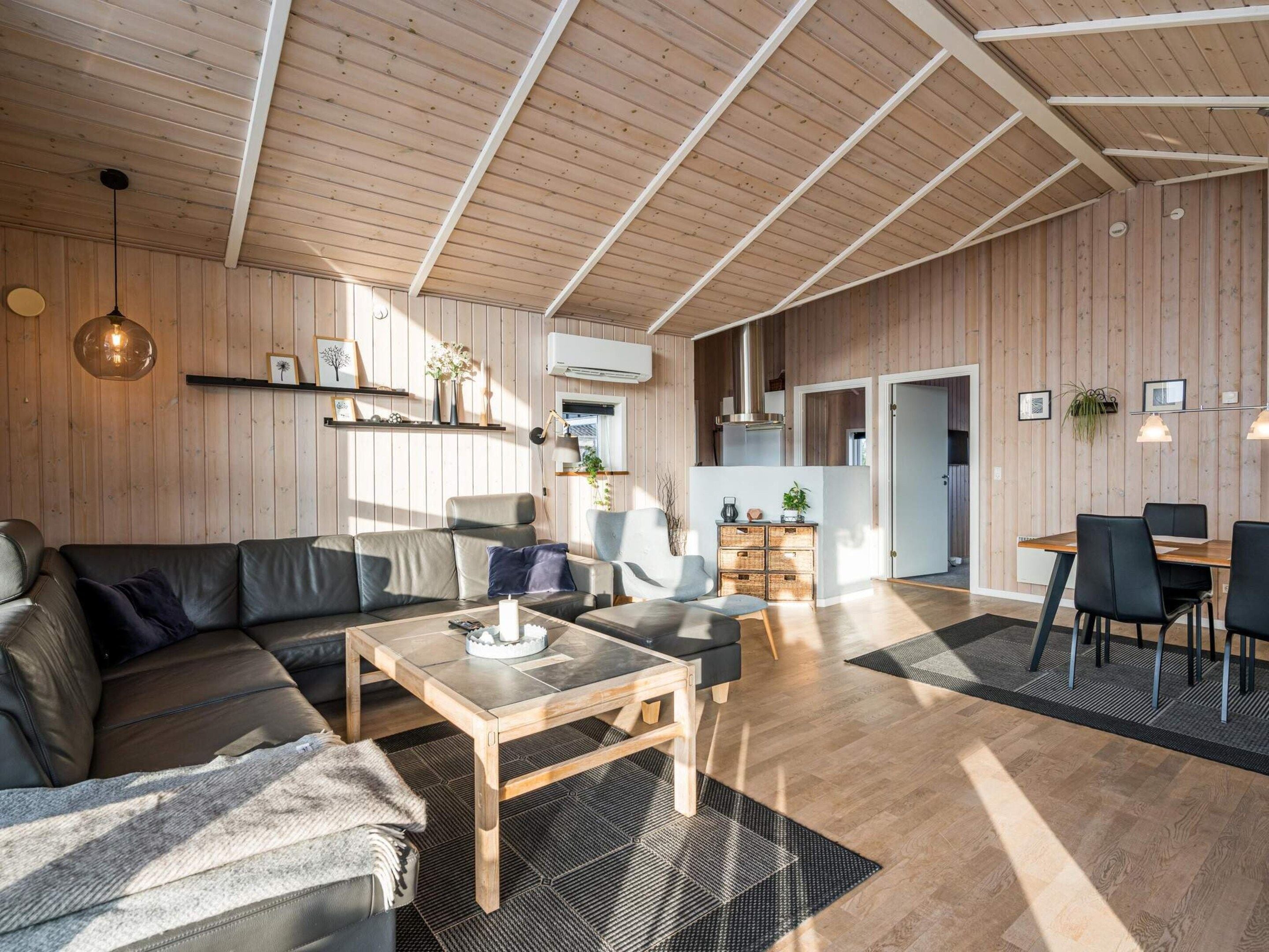 Uma sala ampla com teto de madeira, um sofá, uma mesa de centro e uma área de jantar com cadeiras.