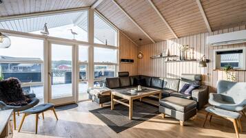 Uma sala de estar moderna com uma janela ampla, teto de madeira e um espaço de estar aconchegante com um sofá e poltronas.