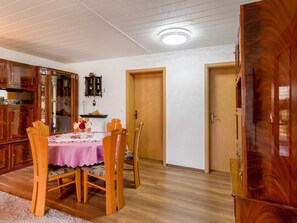 Uma área de refeições com uma mesa e cadeiras de madeira, um armário com portas de vidro e uma luminária no teto.