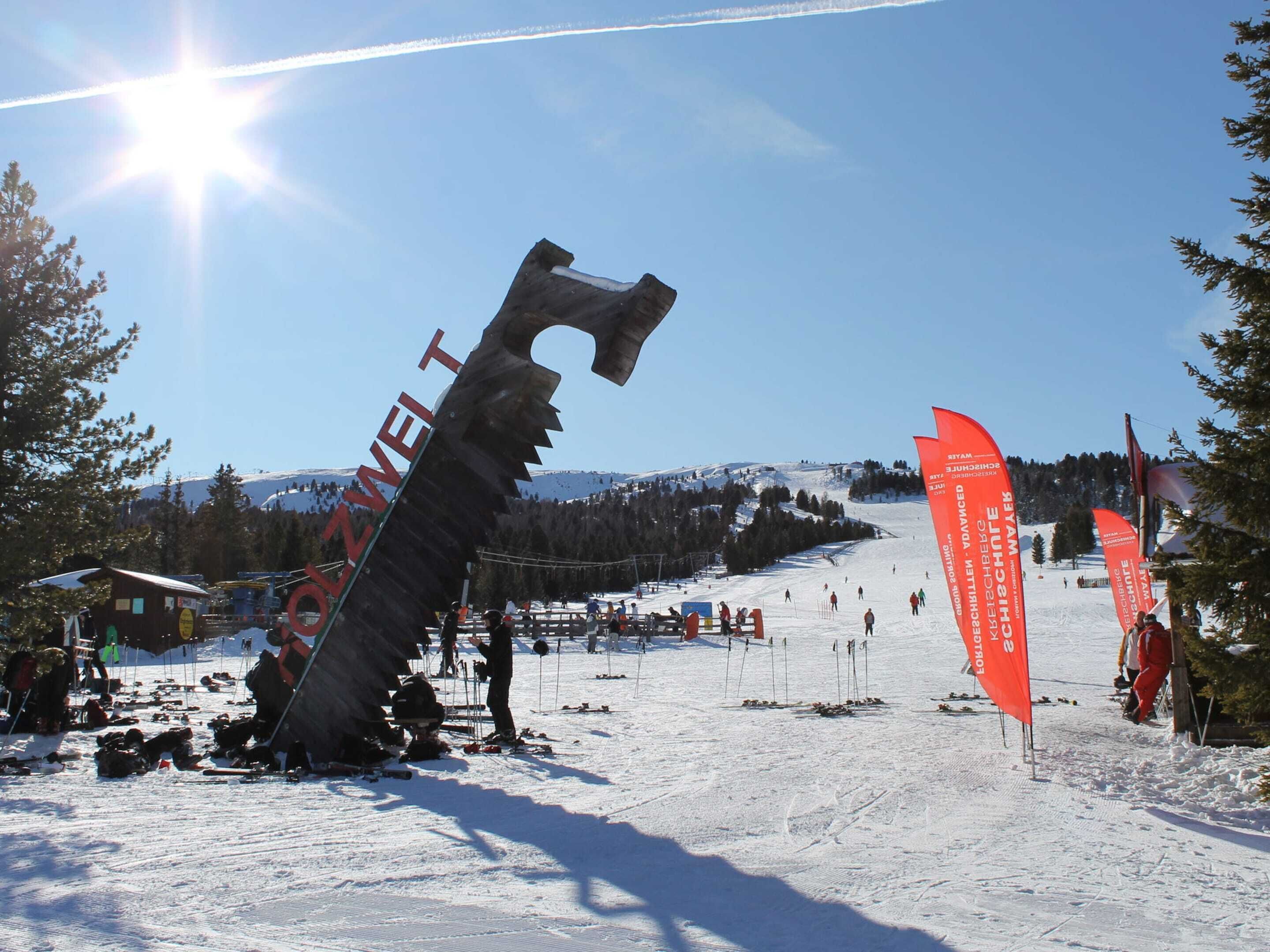 Estância de esqui coberta de neve, com uma grande escultura de machado, equipamentos de esqui e bandeiras.