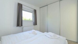 Quarto de hotel com cama, janela com cortinas, radiador e porta deslizante.