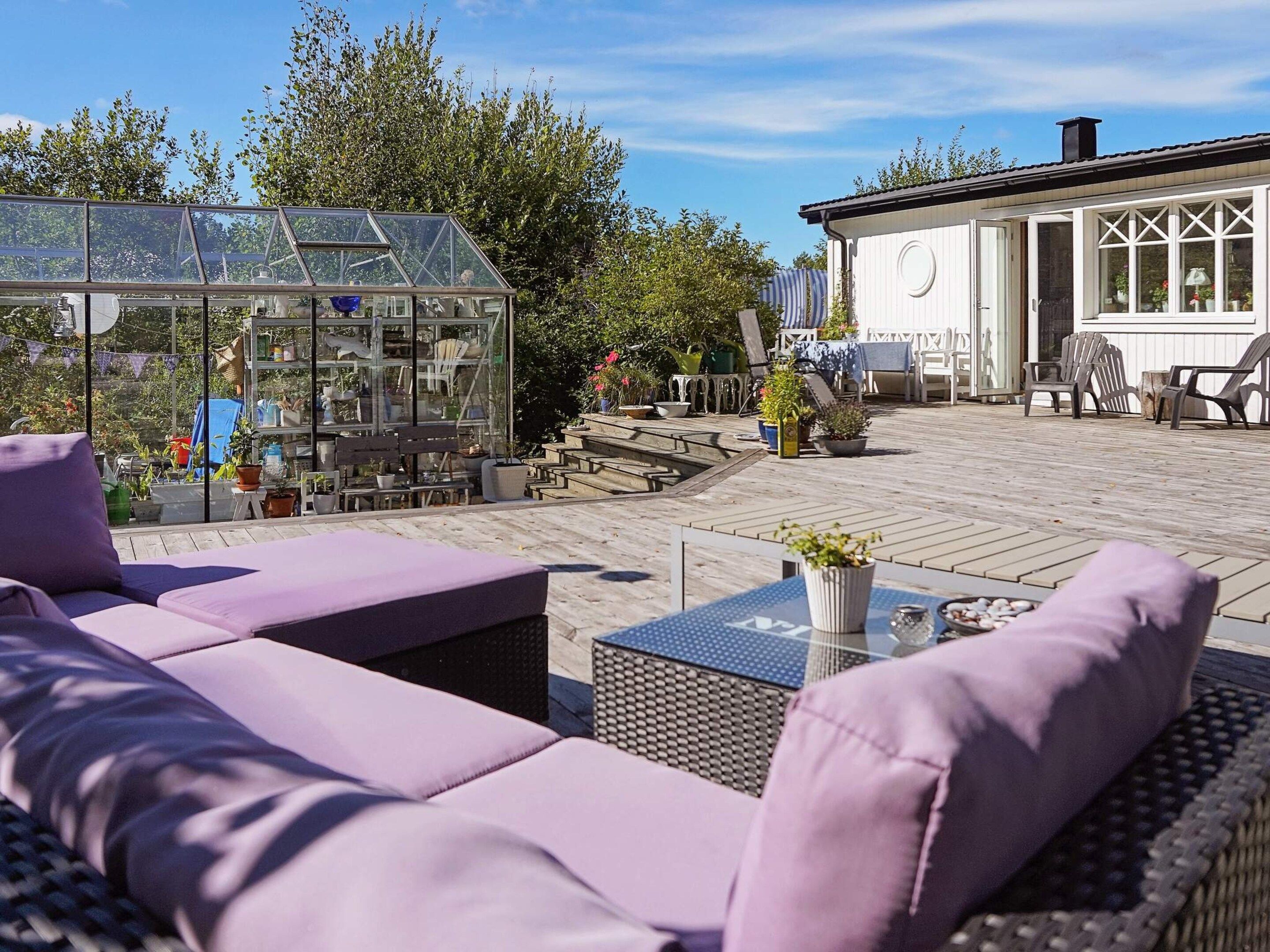 Área de estar ao ar livre coberta, com estrutura tipo estufa de vidro, deck de madeira e mobiliário de lounge.