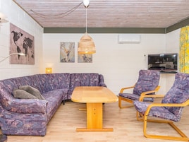 Quarto com sofá seccional, mesinha, duas poltronas, televisão e obras de arte nas paredes.
