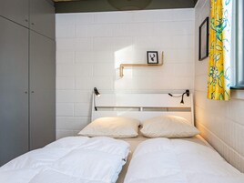 Quarto com duas camas, parede de tijolos brancos, um porta-retrato e cortina amarela.