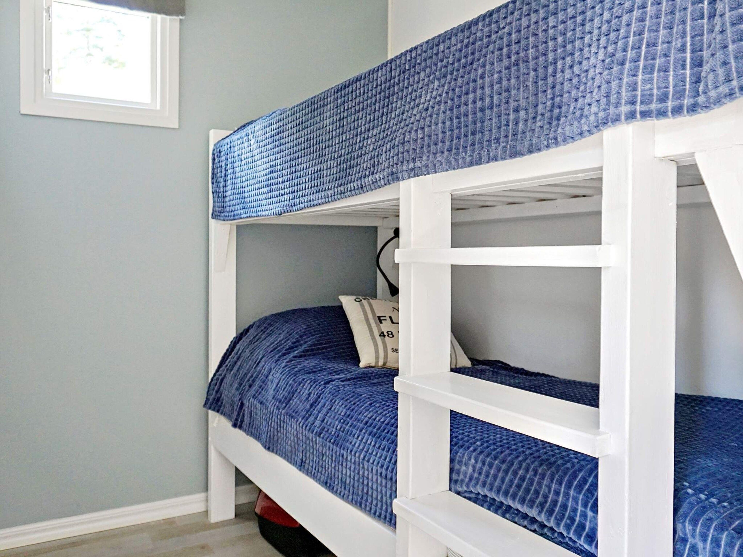 Uma cama beliche com colchão azul e estrutura branca num quarto com paredes azul claro.