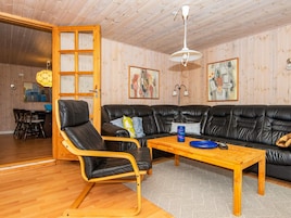 Uma sala de estar mobiliada com sofá, mesa de centro de madeira, poltrona de couro e uma área de jantar com cadeiras e mesa.