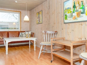 Um quarto com piso de madeira, uma mesa branca com velas, um sofá marrom, uma cadeira de madeira e um quadro na parede.