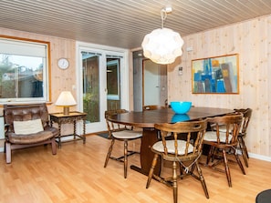 Uma sala de jantar com mesa e cadeiras de madeira, uma tigela azul, um abajur e um quadro na parede.