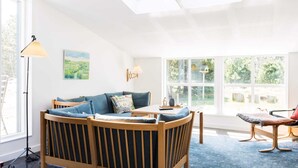 Um quarto luminoso com sofá de madeira, mesa de jantar e janelas amplas.