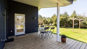 Uma área externa coberta com deck de madeira, uma mesa com cadeiras e um vaso de planta.